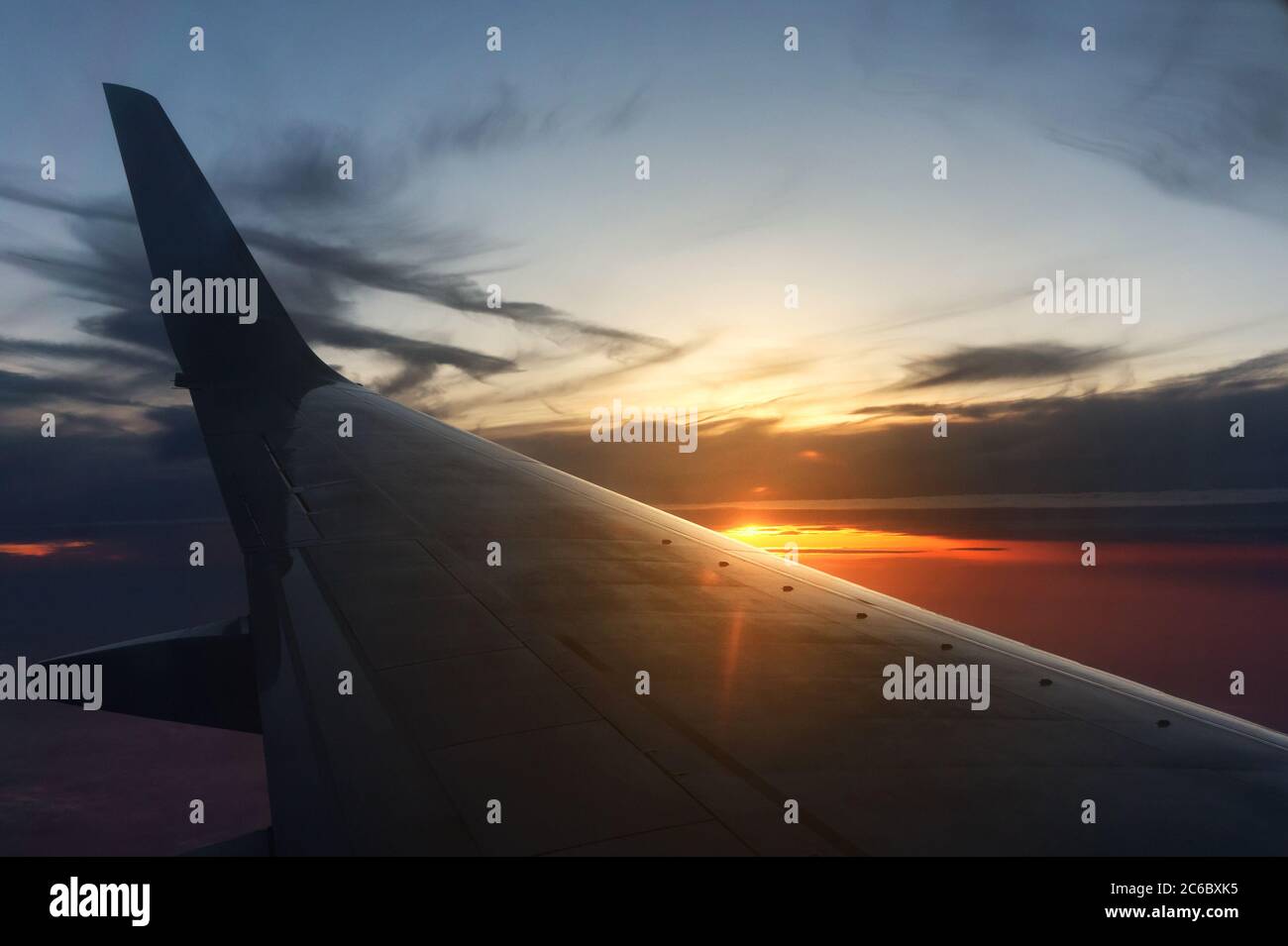 Wing of a flying airplane on the background of the sun rays at sunset ...