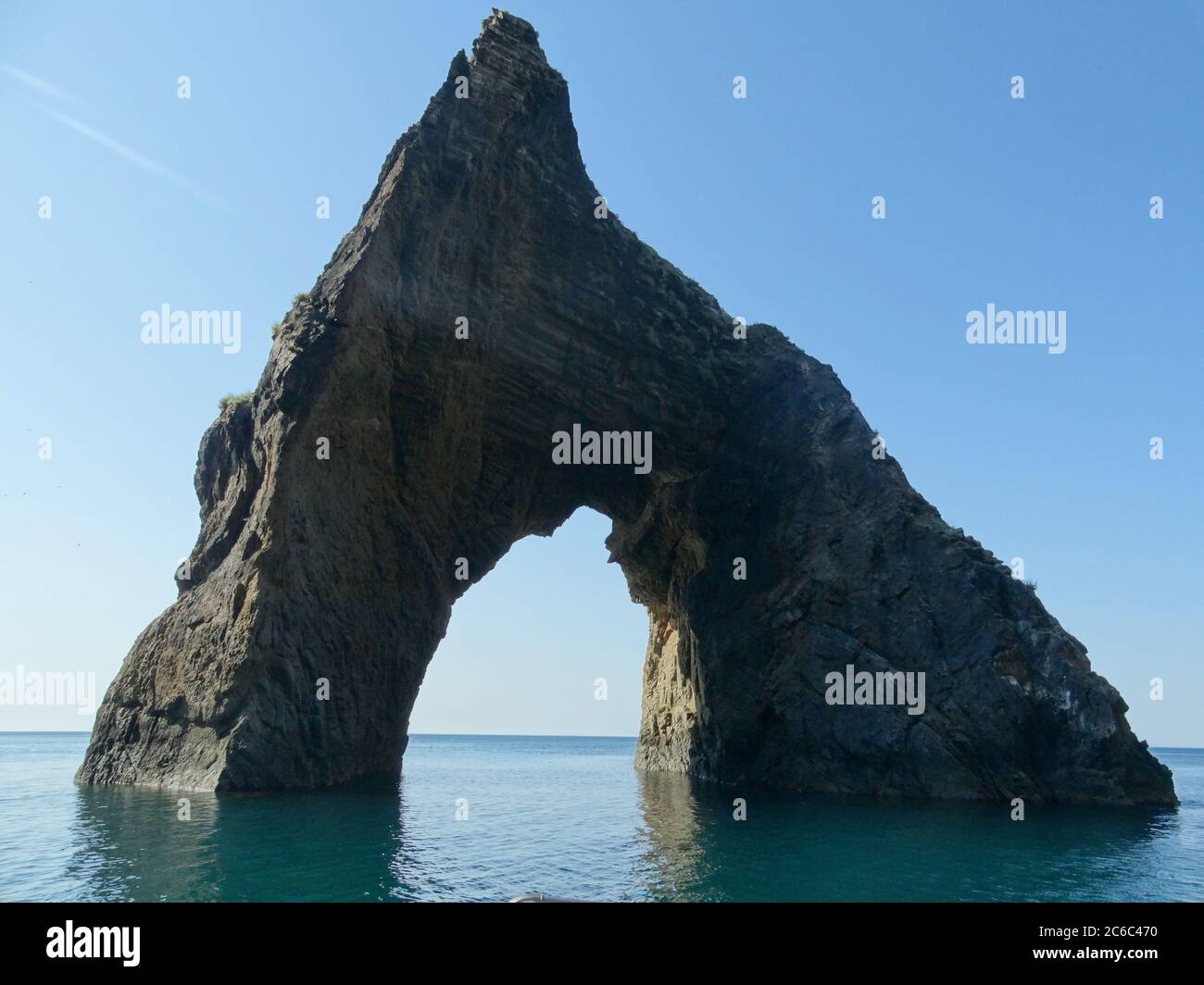 A triangular rock with an arch in the middle protrudes from the sea ...