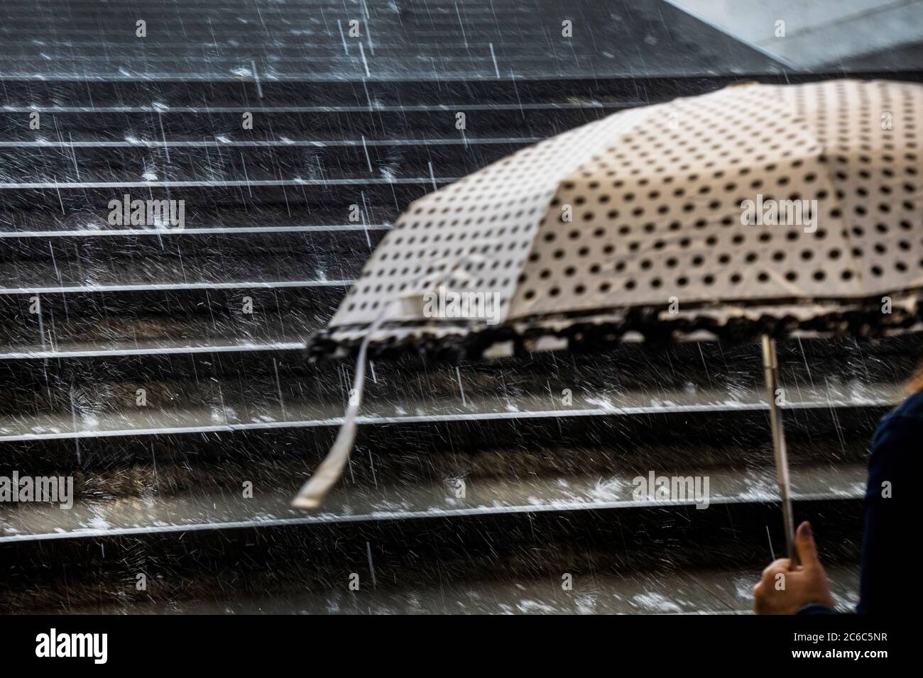 A woman walks in the pouring rain under an umbrella on a pedestrian ...