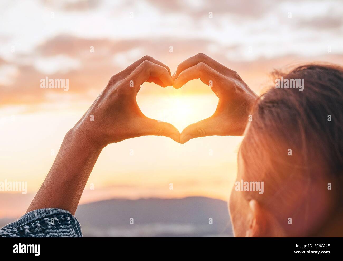 Young female making a HEART shape with her fingers catching the sunset ...
