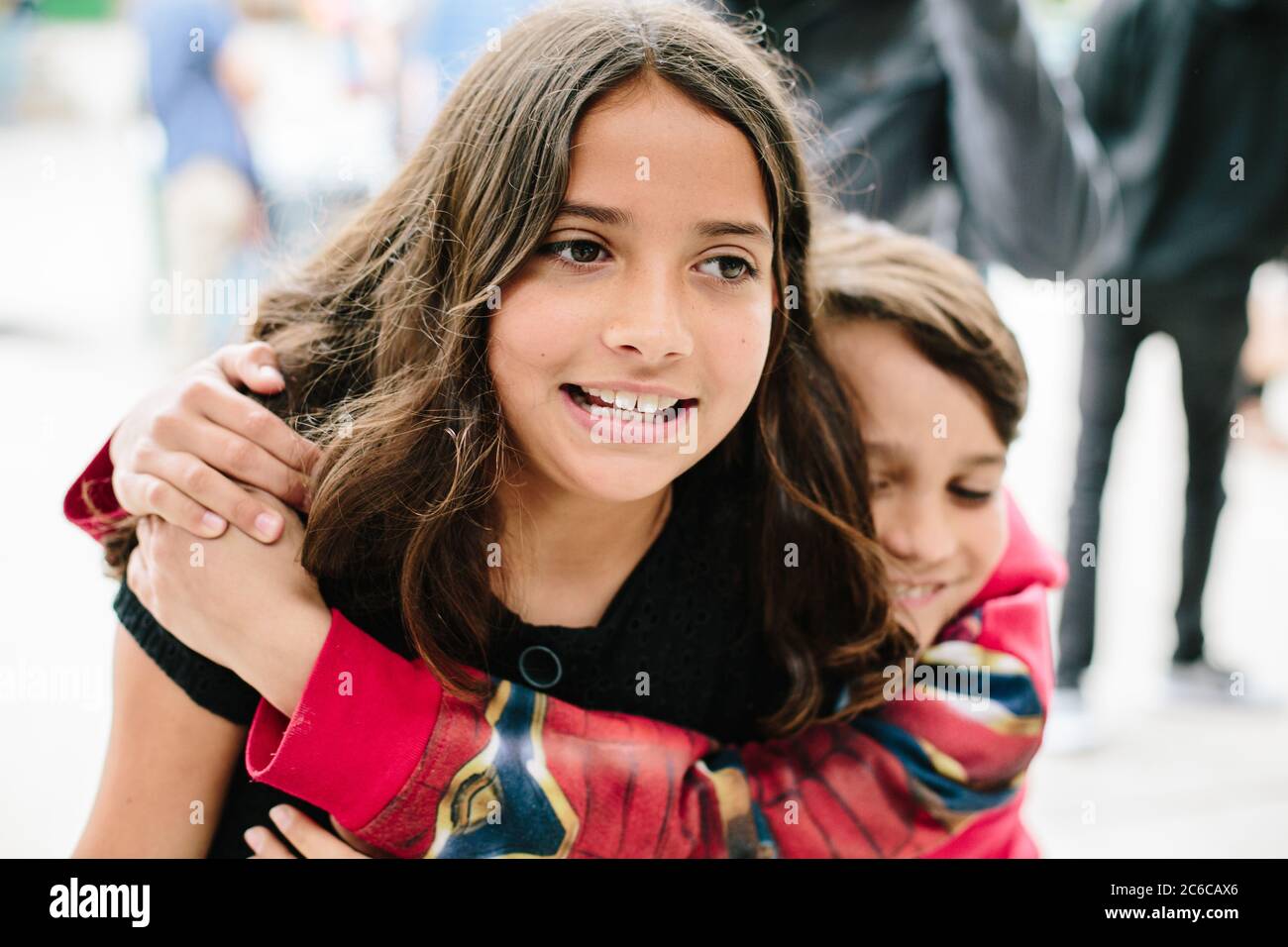 Boy happily hugs girl from behind while she smiles looking overwhelmed ...