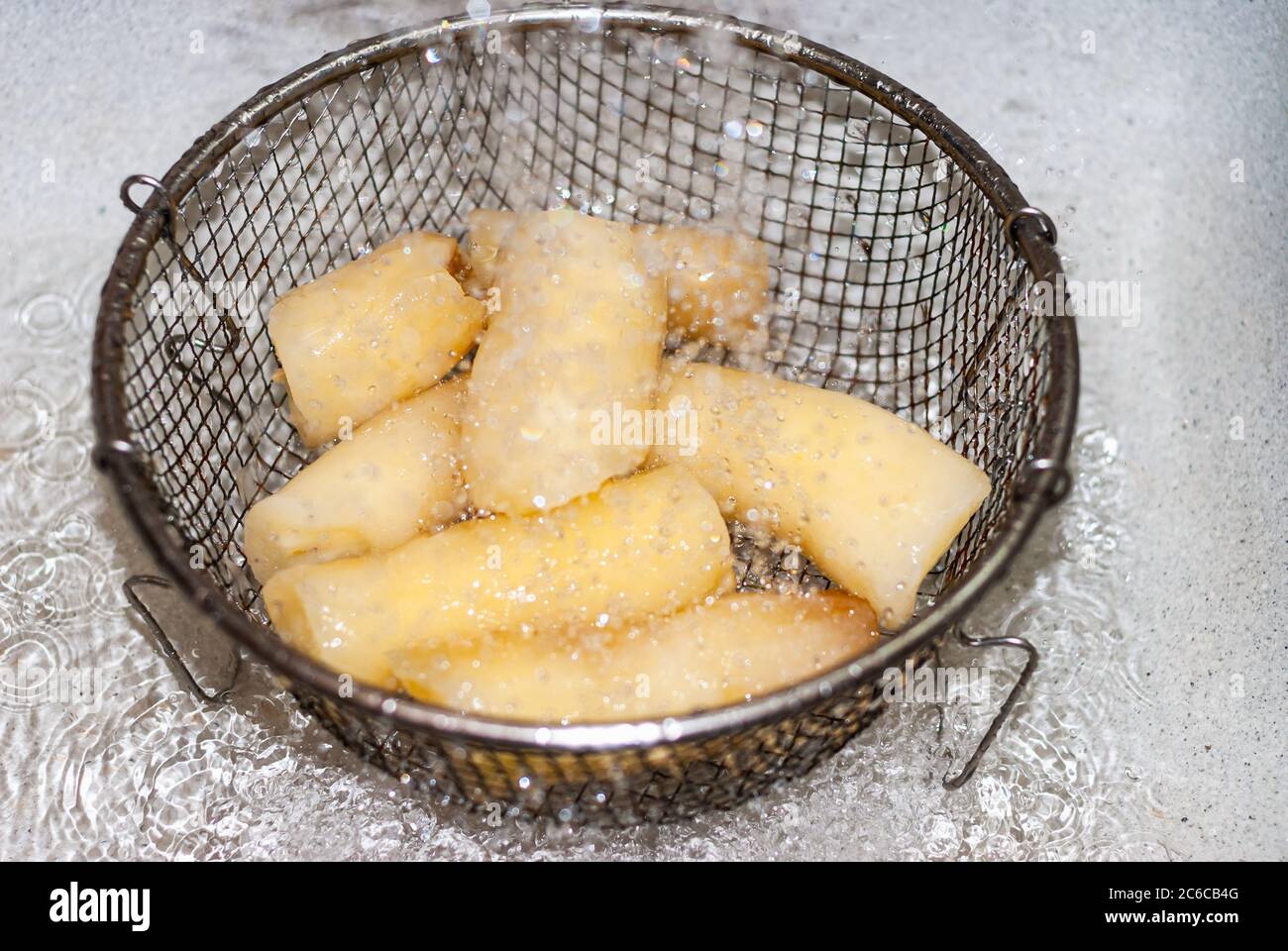 washing cassava with water in a metal strainer, Manihot esculenta ...