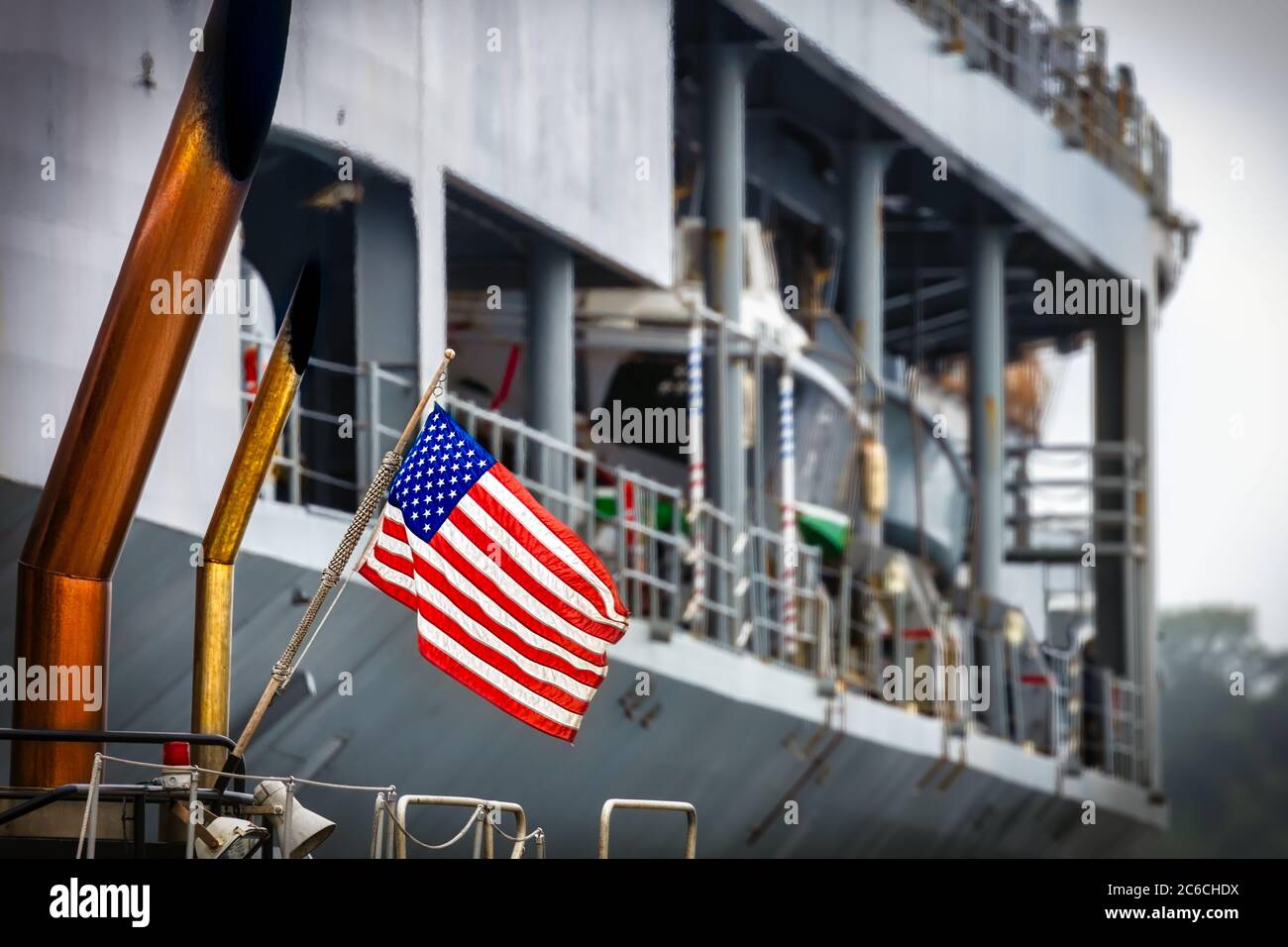 The American flag of a US Navy tugboat as it pushes a ship to its dock ...
