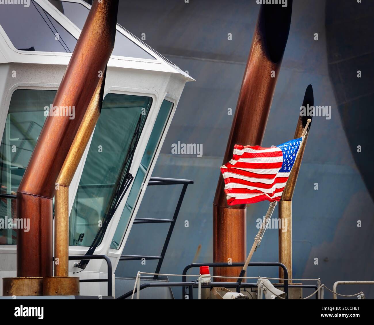 The American flag of a US Navy tugboat as it pushes a ship to its dock ...