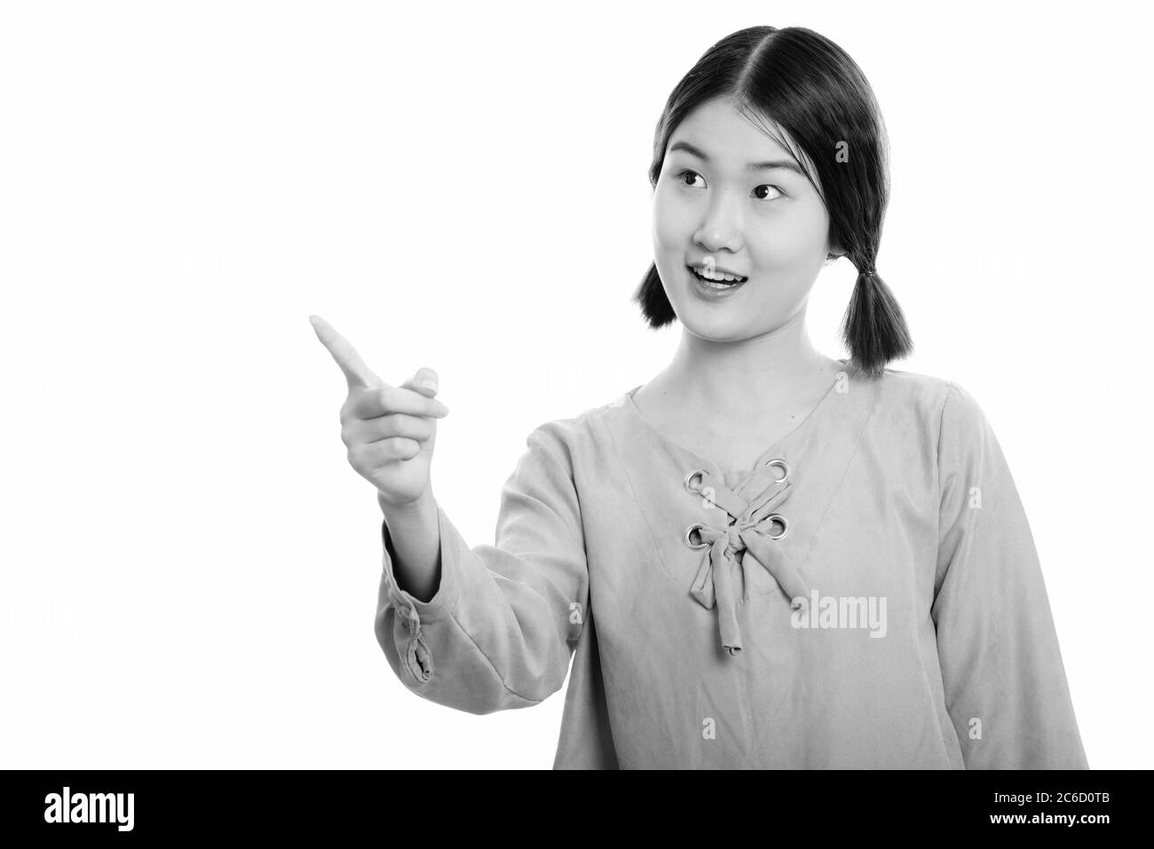 Studio shot of young beautiful Asian woman pointing finger at distance ...
