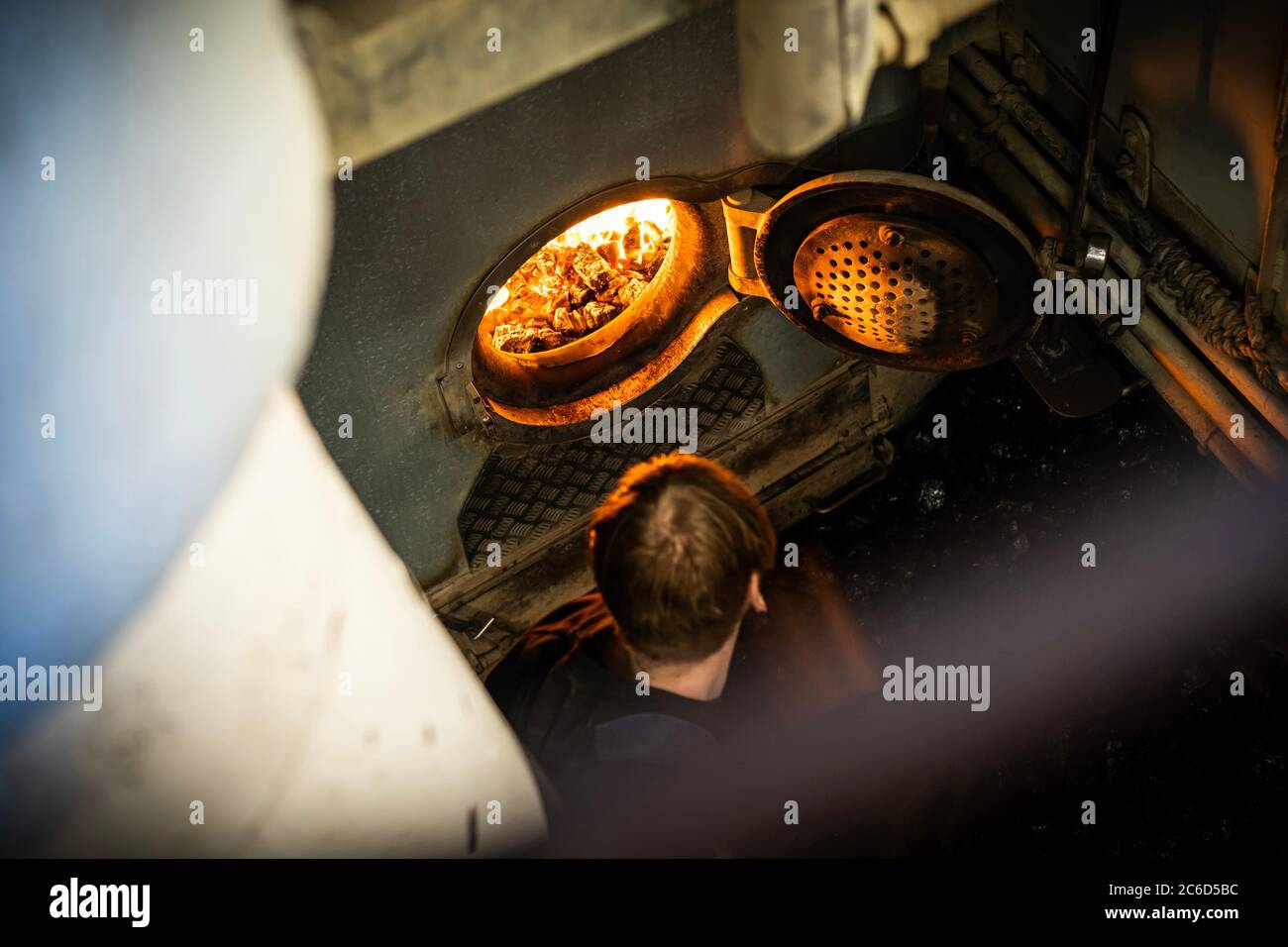 A worker insert a coal inside the engine of coaled power steam ship ...