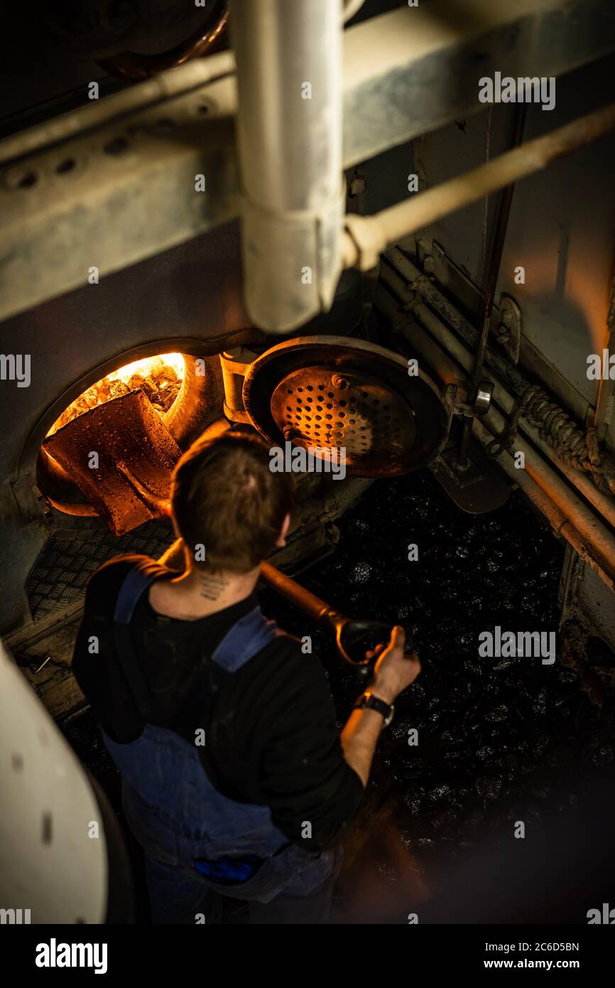 A worker insert a coal inside the engine of coaled power steam ship ...