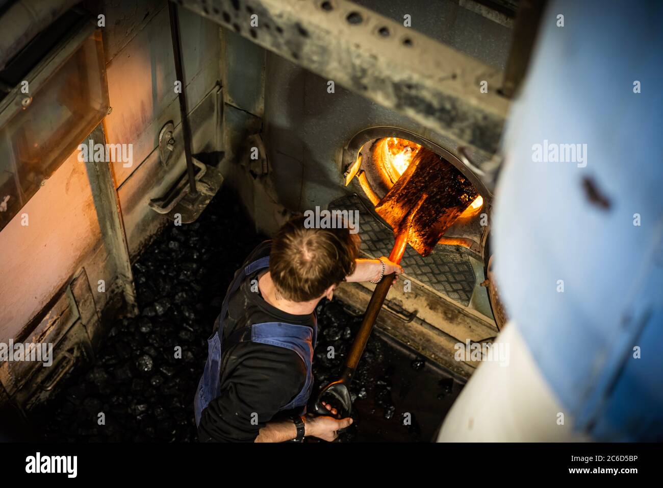 A worker insert a coal inside the engine of coaled power steam ship ...