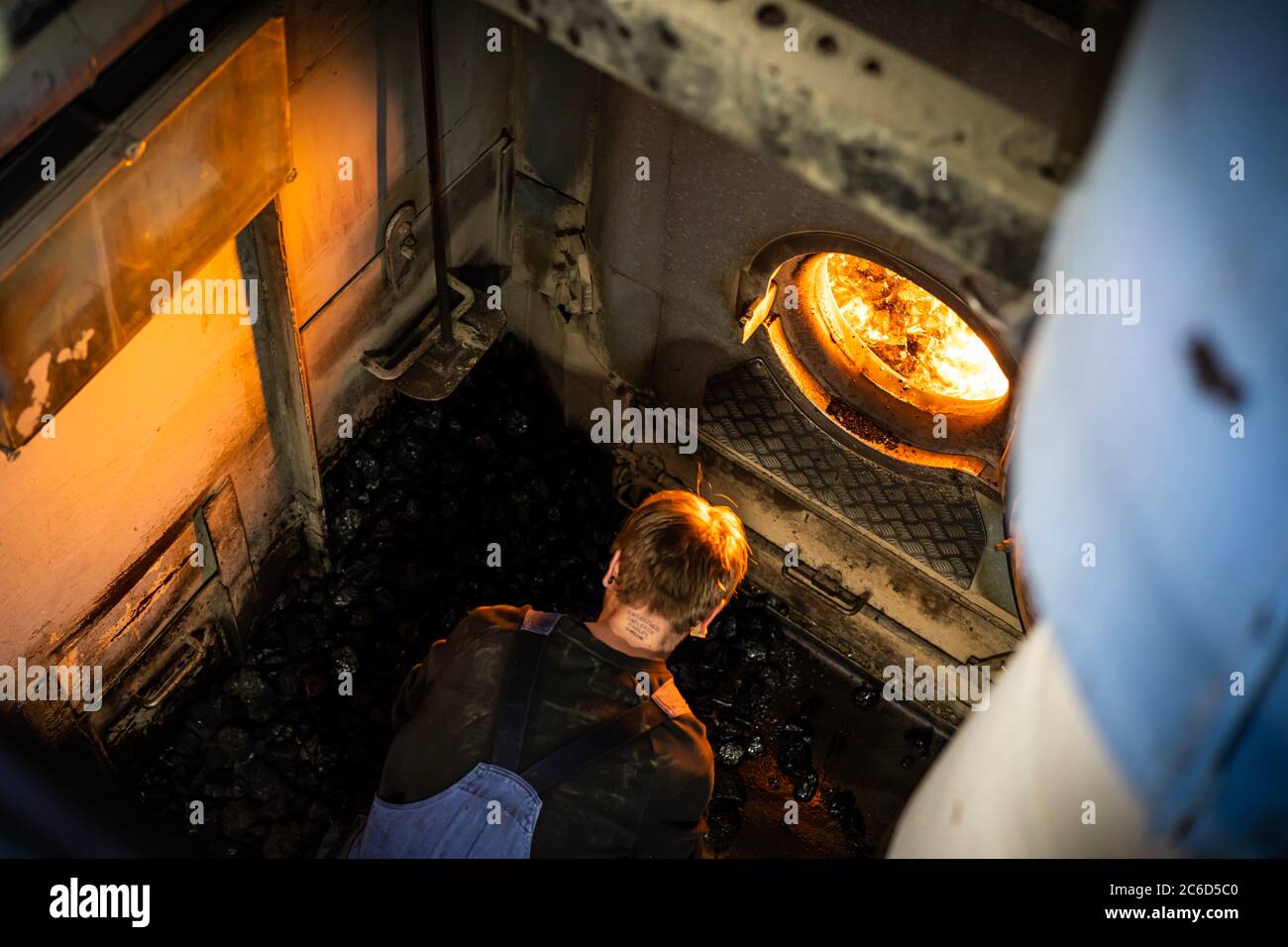 A worker insert a coal inside the engine of coaled power steam ship ...