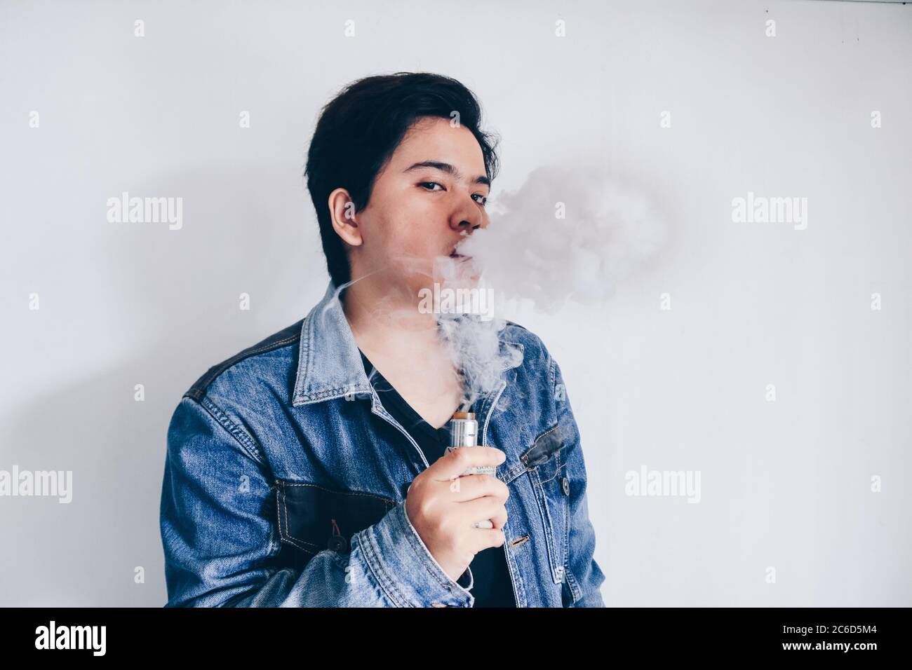 Asian beautiful short hair girl wear jeans jacket is smoking electronic ...