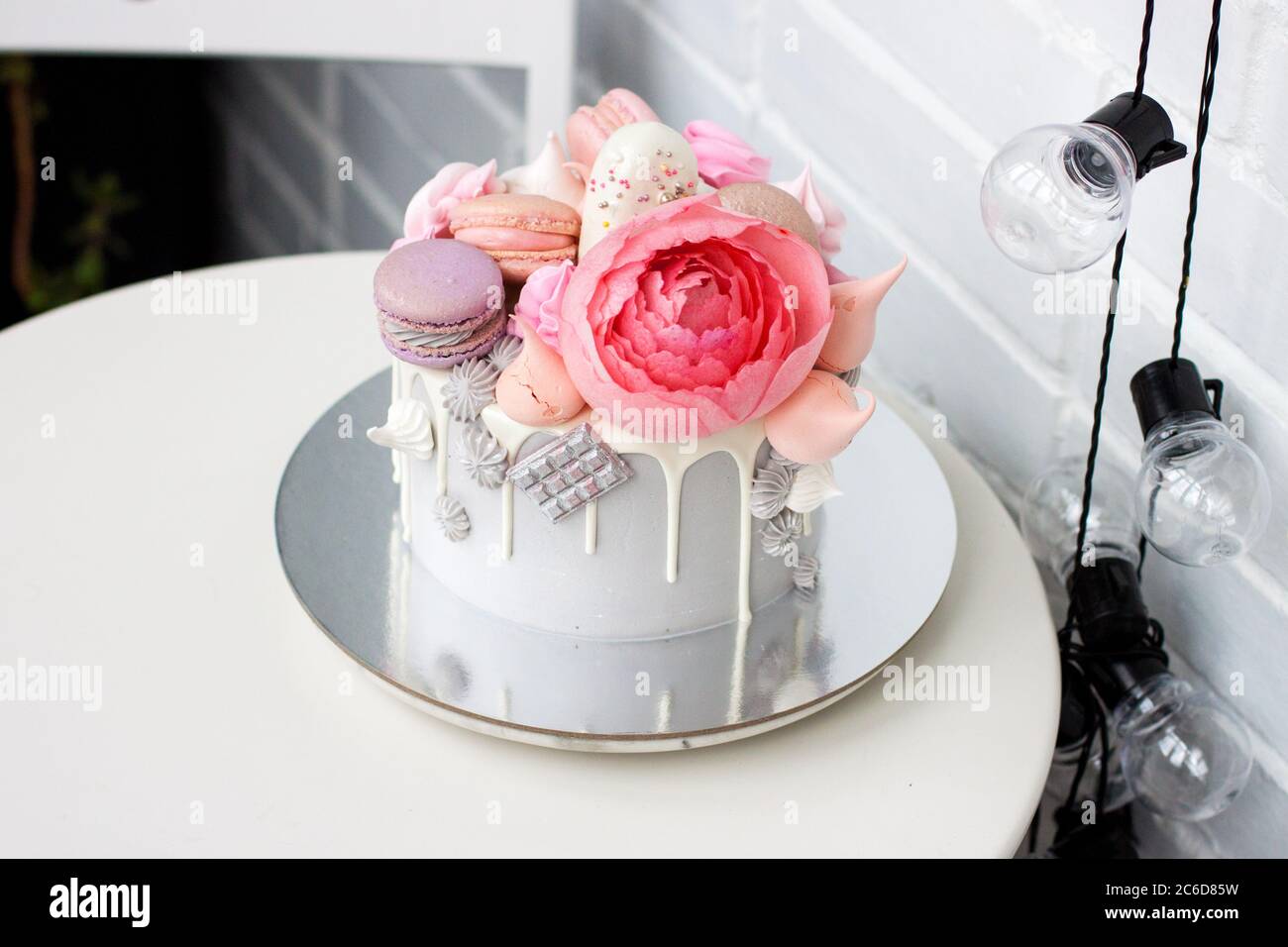 Modern grey cake with pink peony flowers, chocolate and macaroons for a ...