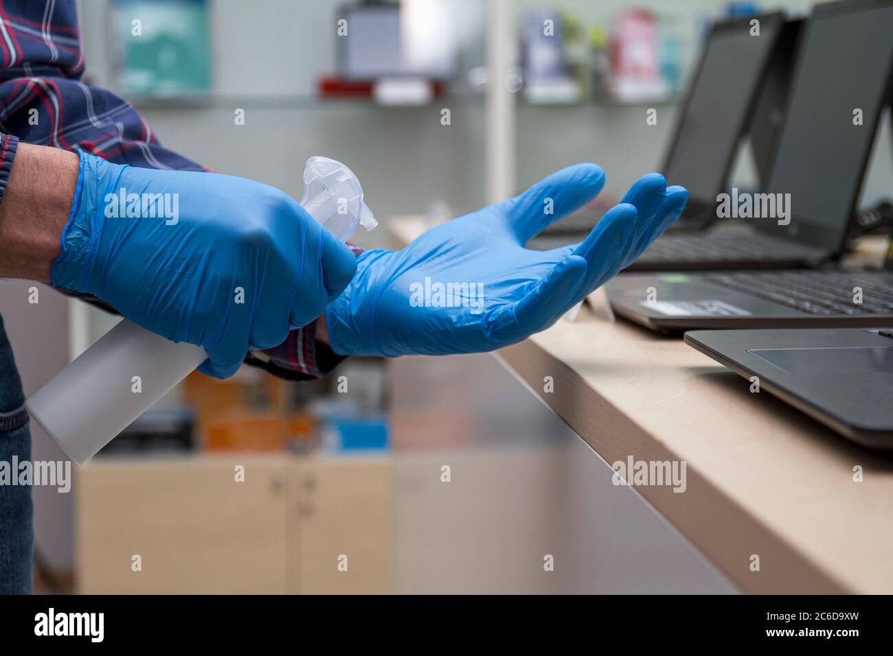 Man in blue protective gloves disinfects his hands in a computer store ...