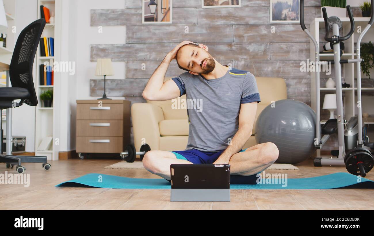 Guy stretching neck muscle watching online fitness lesson on tablet ...