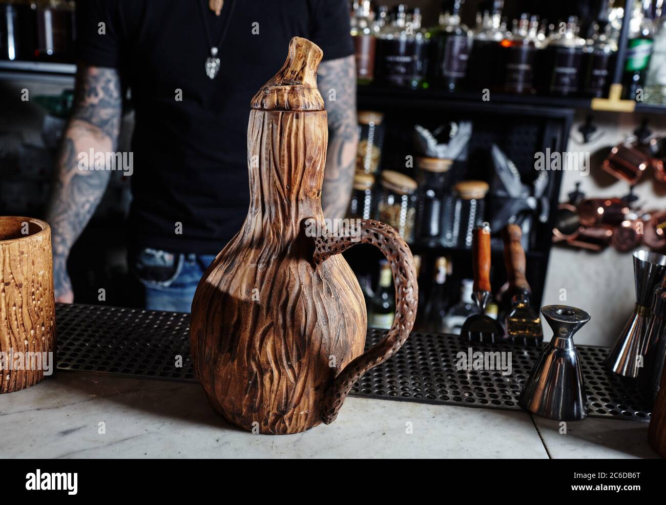 A male bartender making a cocktail on the bar counter. Clay jug with ...
