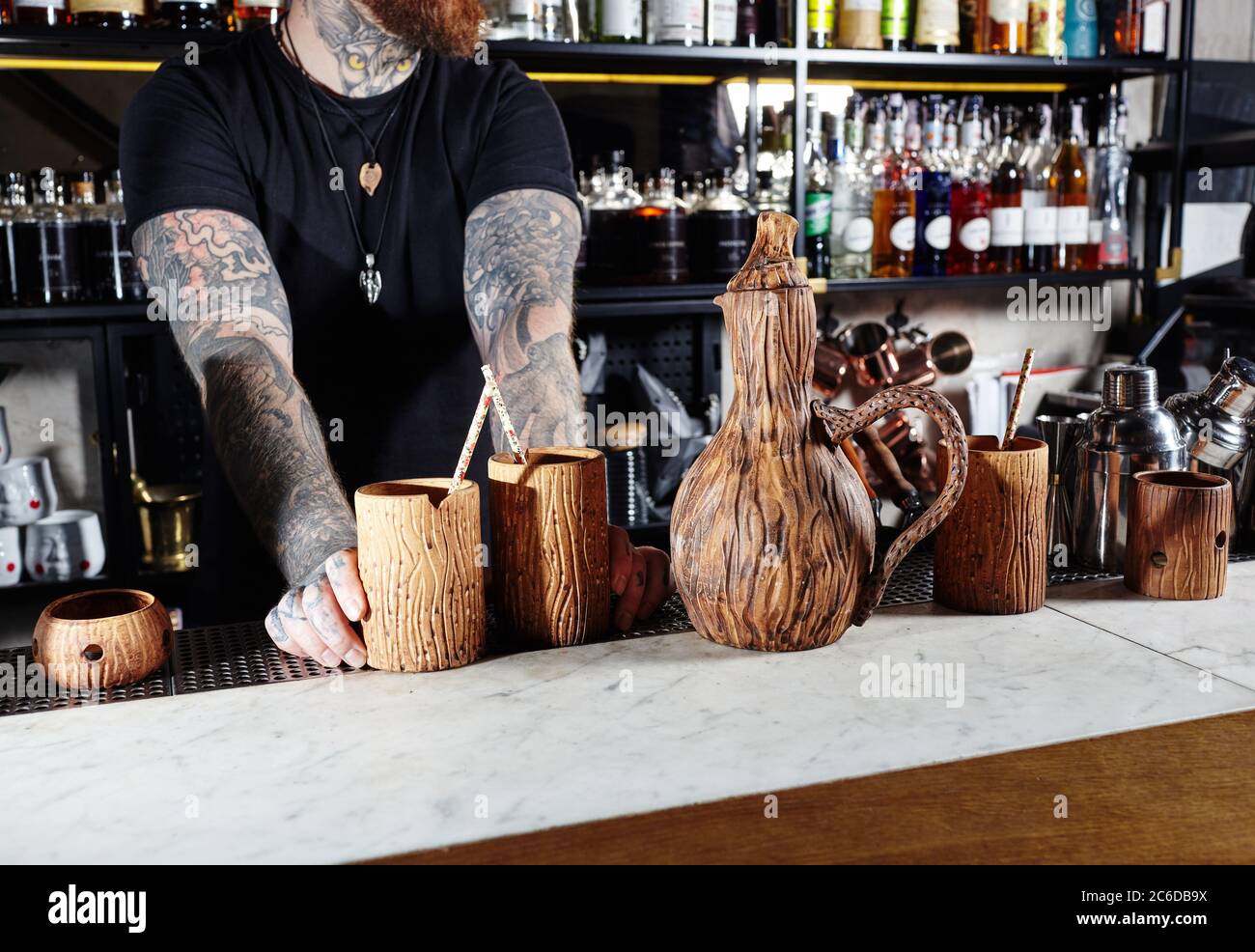 A male bartender making a cocktail on the bar counter. Clay jug with alcohol beverage.Process of ...