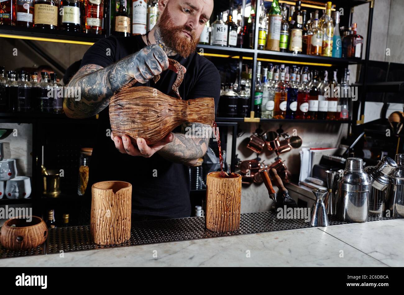 A male bartender pours from a clay jug into a ceramic cup. Making a ...