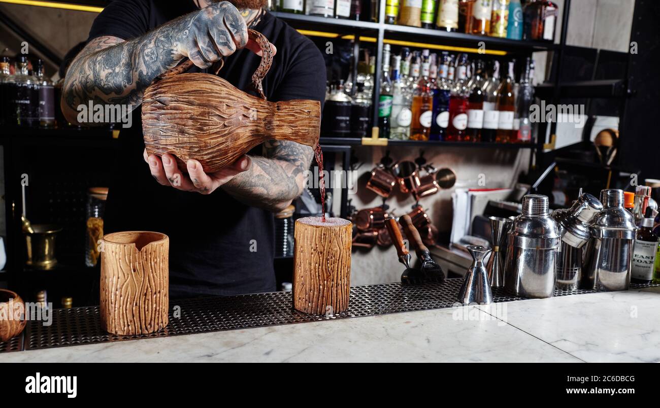 A male bartender pours from a clay jug into a ceramic cup. Making a ...