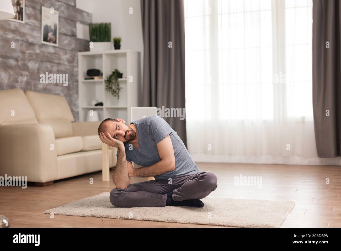 Bored man sitting on carpet in living room during self isolation Stock ...