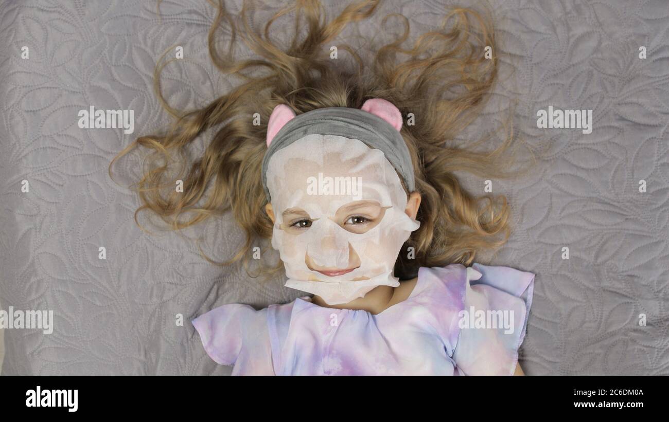 Pre-teen cute girl with cloth moisturizing face mask on face laying on ...