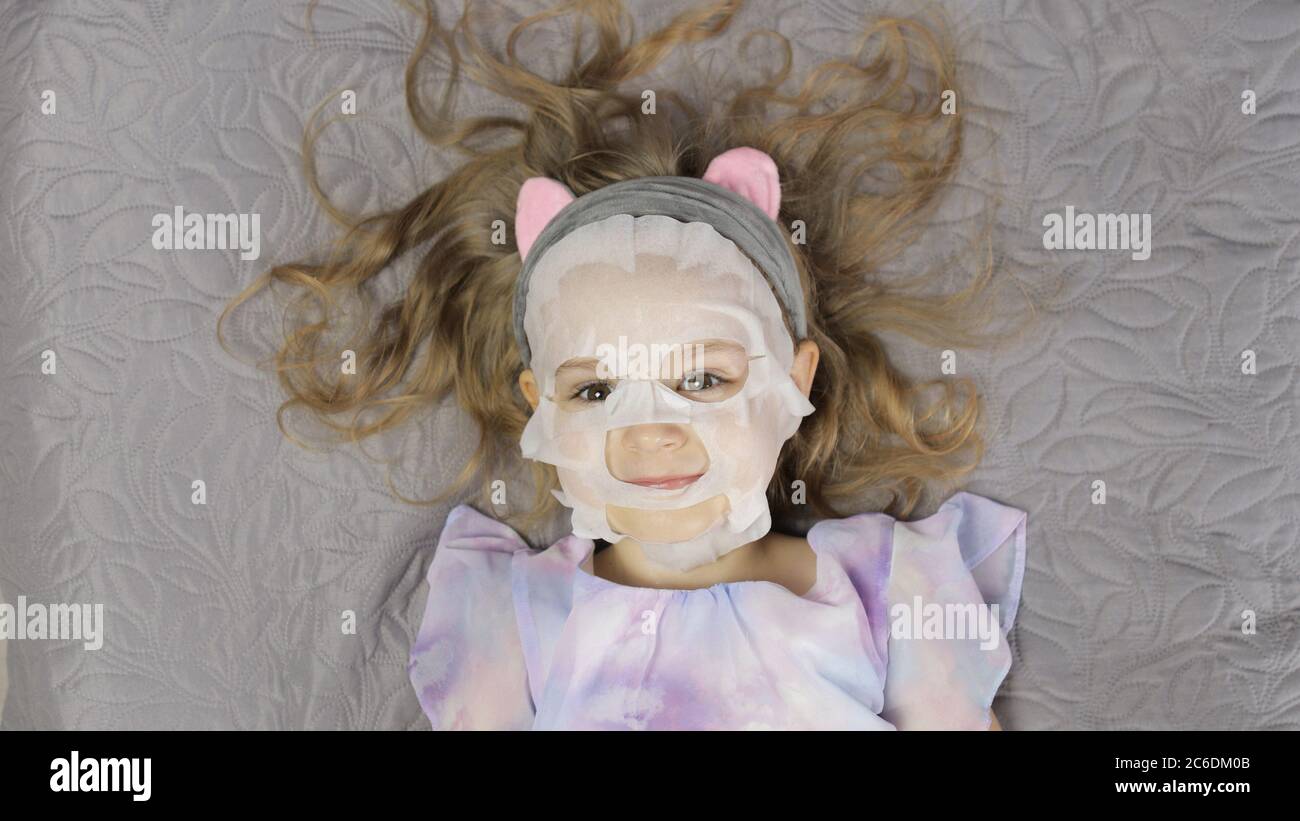 Pre-teen cute girl with cloth moisturizing face mask on face laying on ...