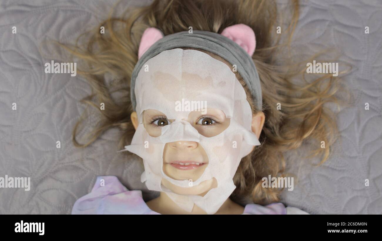 Pre-teen cute girl with cloth moisturizing face mask on face laying on ...