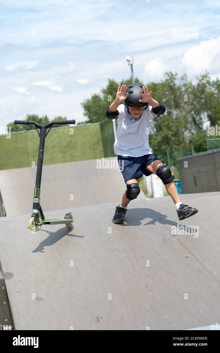 Fall while jumping. A cute little boy rides a scooter in a skatepark. A ...