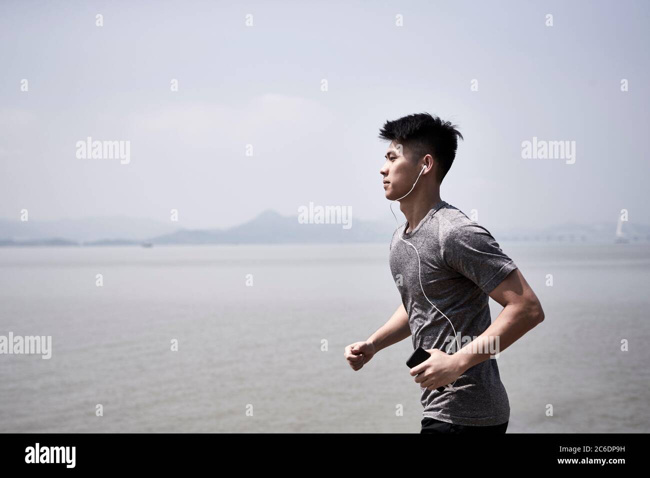young asian adult man running jogging outdoors by the sea, side view ...