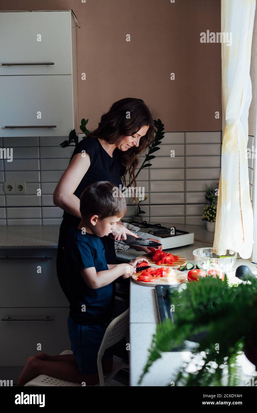 Little son helps mom cook vegetable salad cuts vegetables in kitchen ...