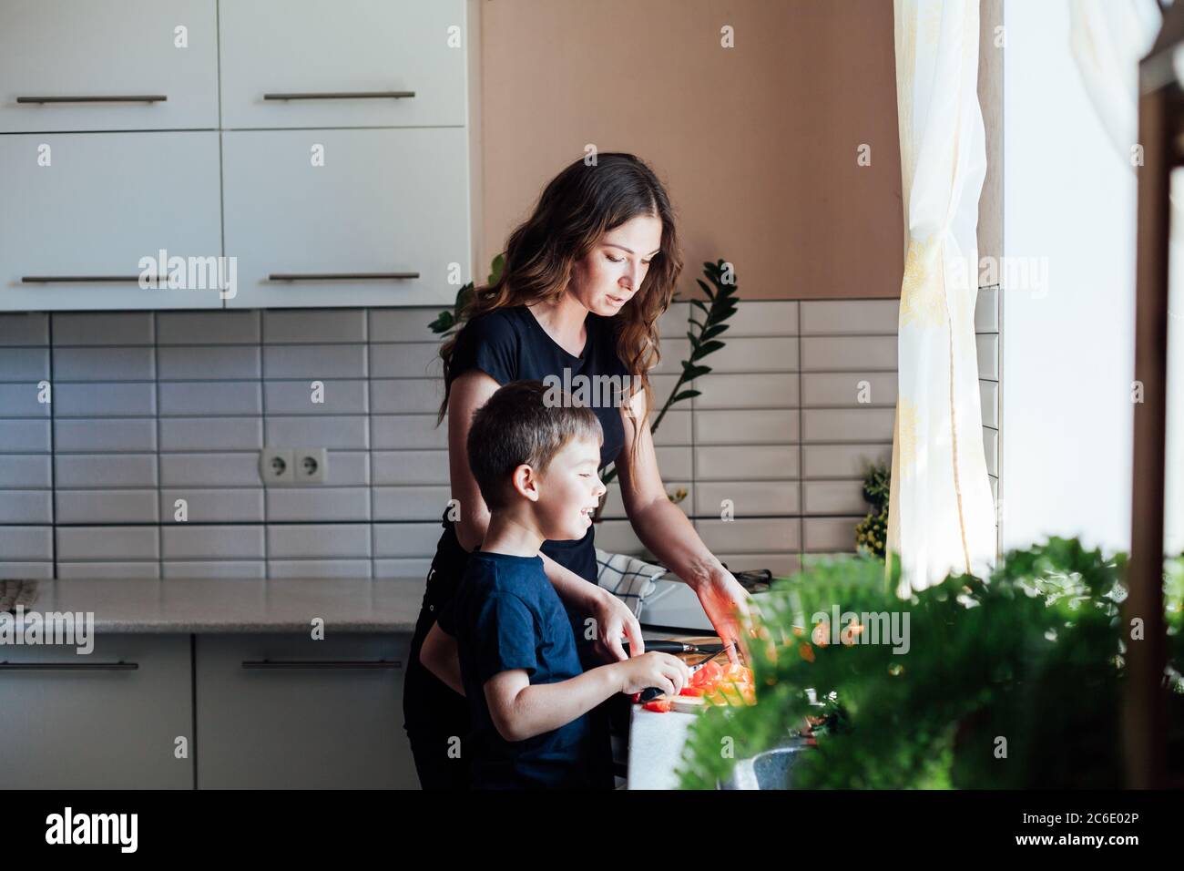 Little son helps mom cook vegetable salad cuts vegetables in kitchen ...