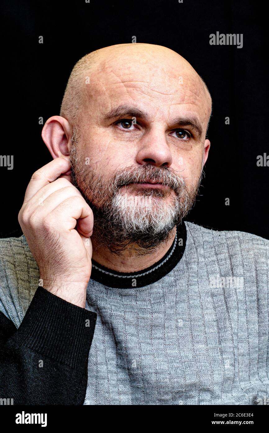 middle-aged bald bearded man touches his ear on a dark background Stock ...