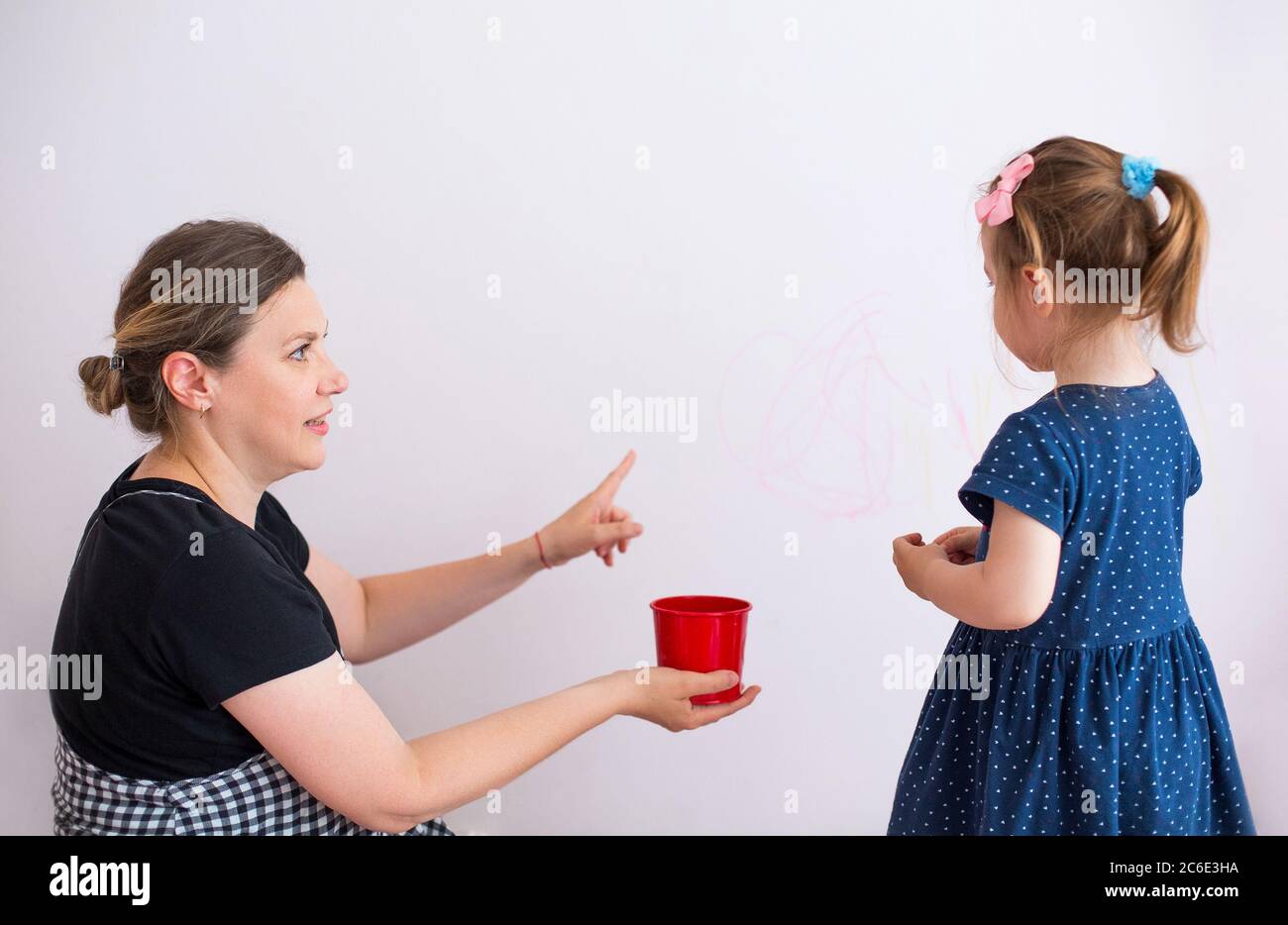 Side view of woman scolding little girl for painting walls in modern ...