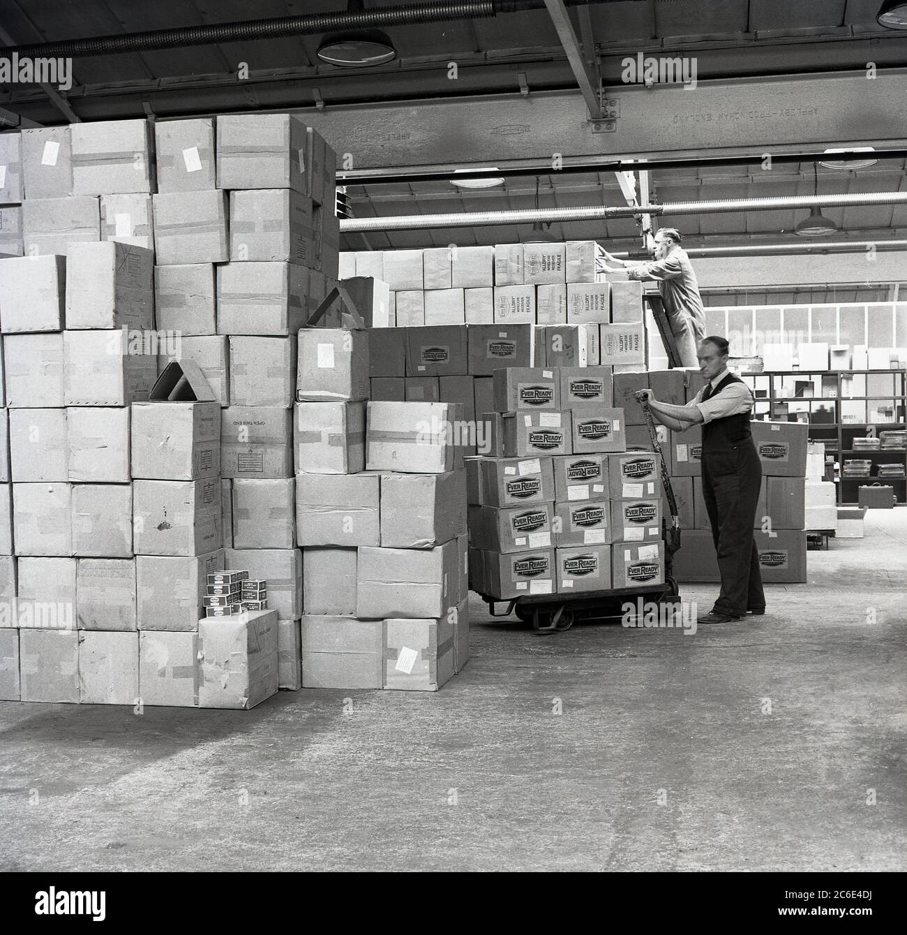 1950s, historical, inside a warehouse, two male employees moving boxes ...