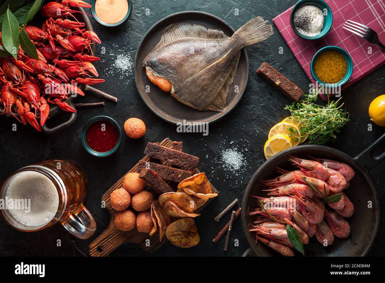 Grilled shrimps, crayfish, flatfish on a board and beer mug. Dark ...