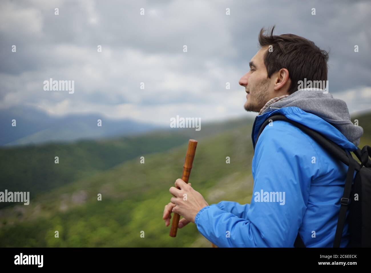 A side view of a young male tourist playing a wooden reed-pipe/ flute ...