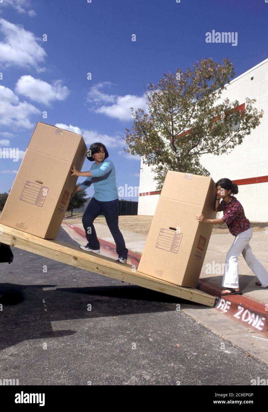 Two 14-year-old Hispanic girls push boxes up inclined plane into back ...