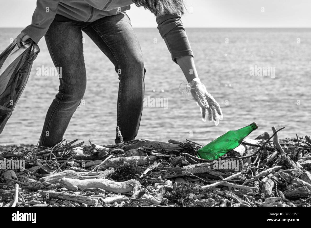 A young woman collects dirty bottles on the beach. Cleaning and ...