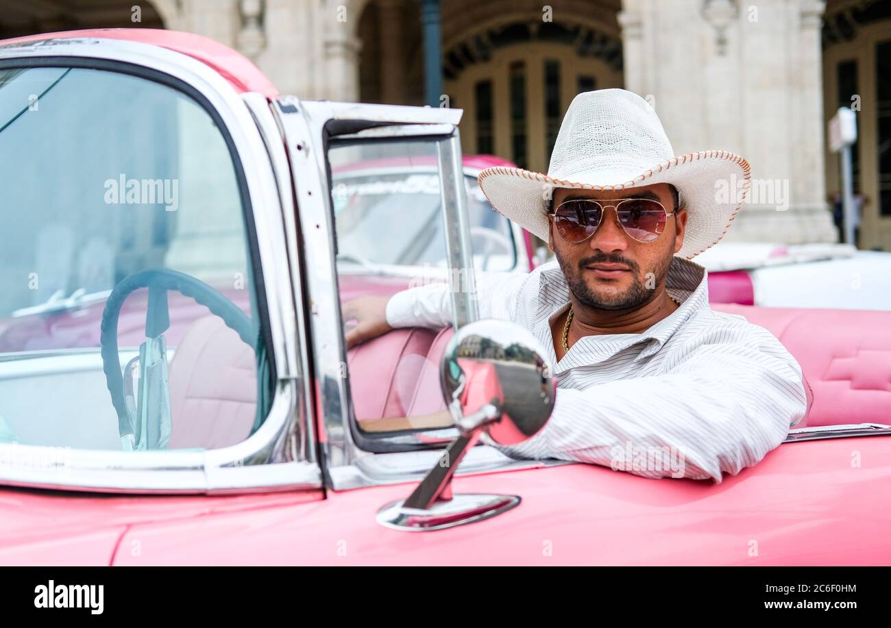 A Cuban man sits inside a classic vintage car on the side of the street ...