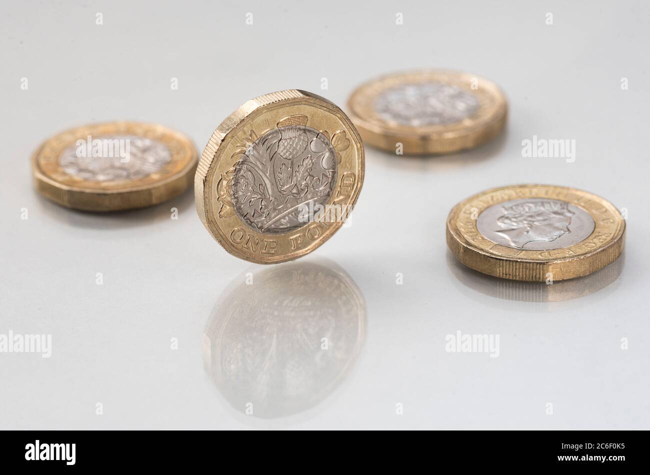 Still life of four one pound coins on a reflective white background ...
