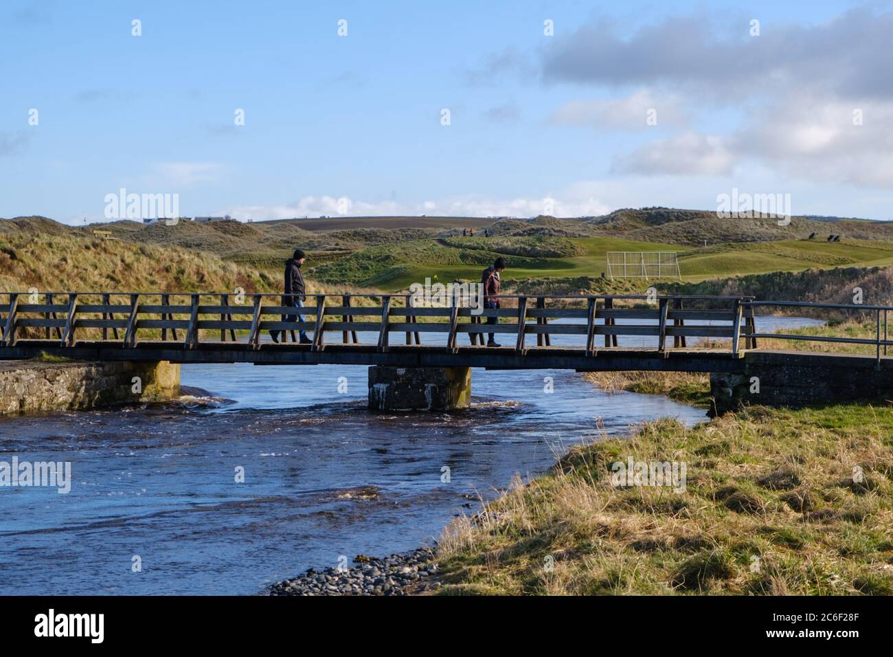 Couple walk across the bridge over the River Bush at Portballintrae in ...