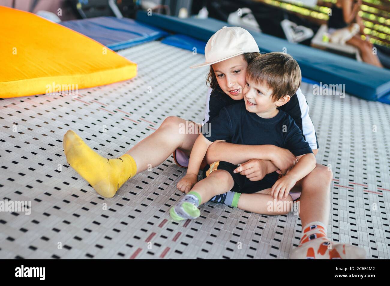 Two Caucasian brothers boys enjoy sitting on a trampoline in an embrace ...