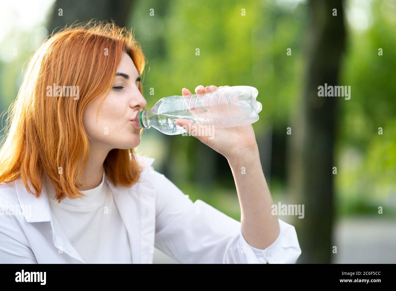 Happy thirsty redhead woman drinking fresh bottled water in summer ...