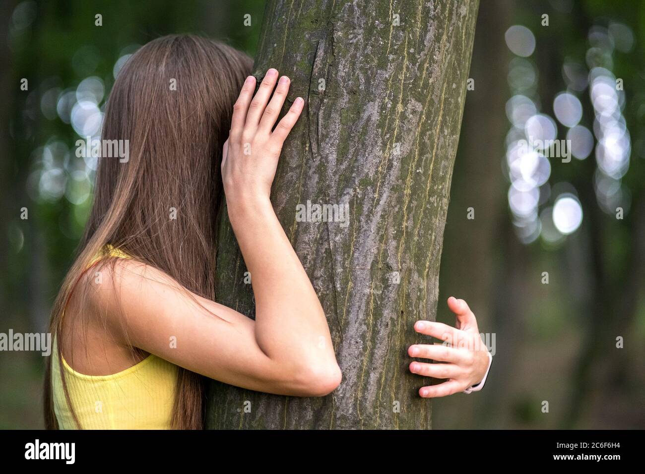 Lonely young woman leaning to tree trunk with her hands in summer ...