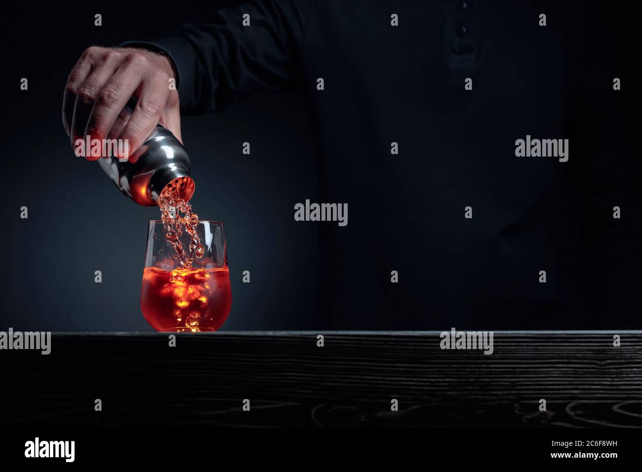 Bartender pouring cocktail into glass at bar counter. Alcoholic drink pouring from a shaker into ...
