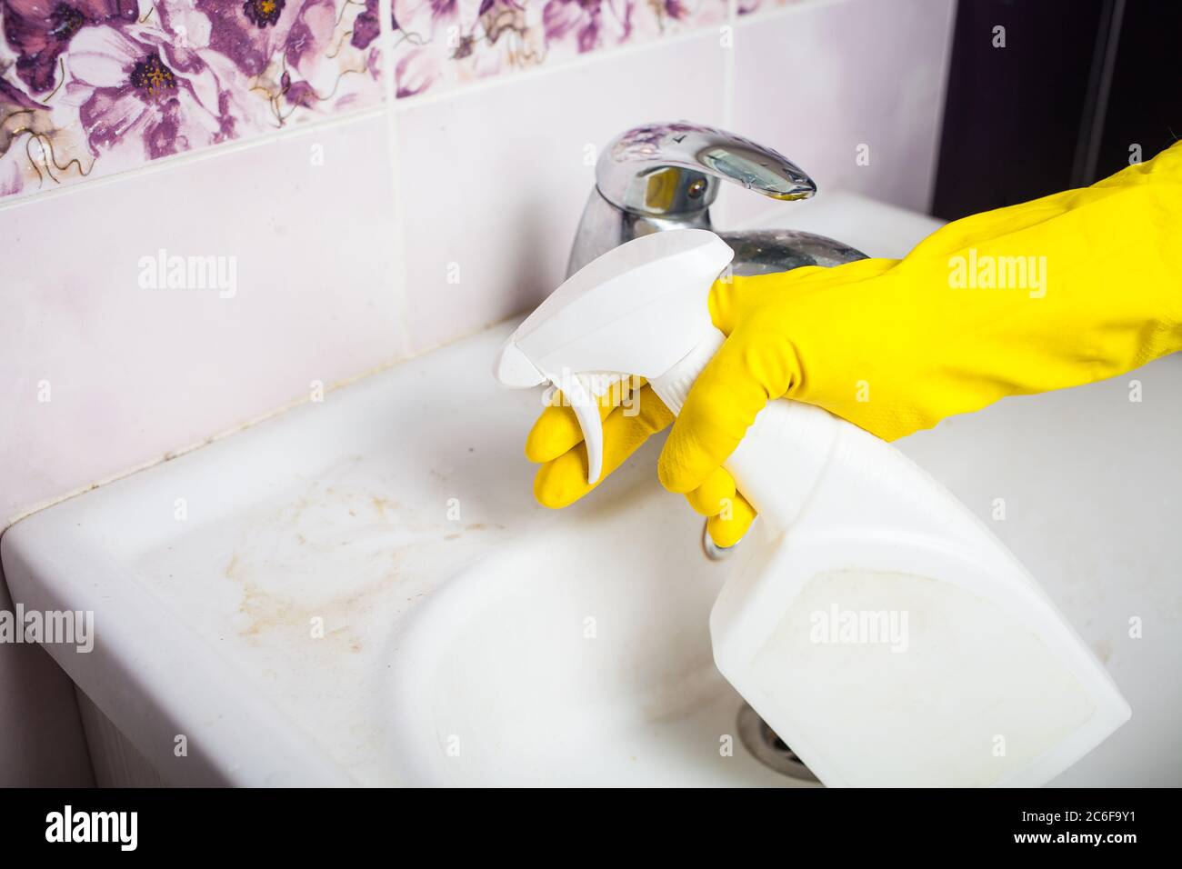Maid with rubber glove cleaning tap and sink. Housekeeping scrubbing ...