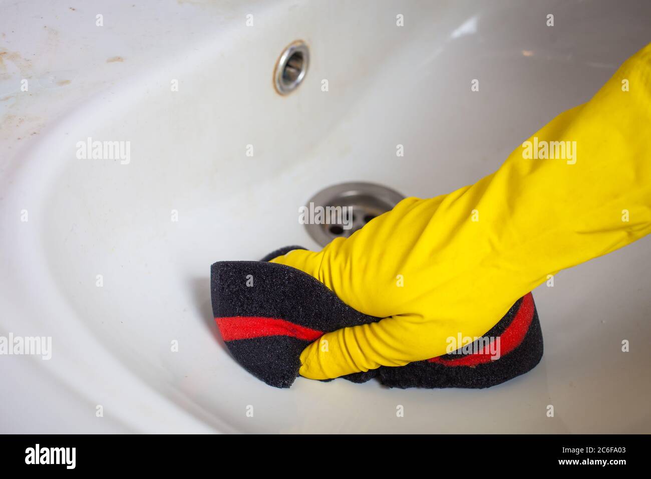 Maid with rubber glove cleaning tap and sink. Housekeeping scrubbing ...