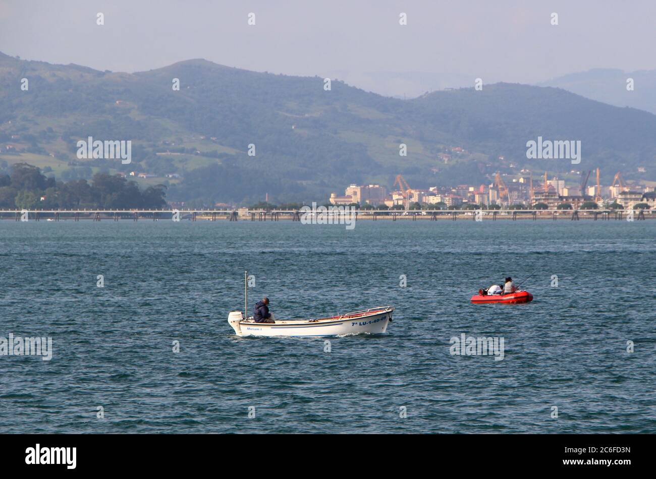 Small white open boat with outboard motor passing a small orange rubber ...
