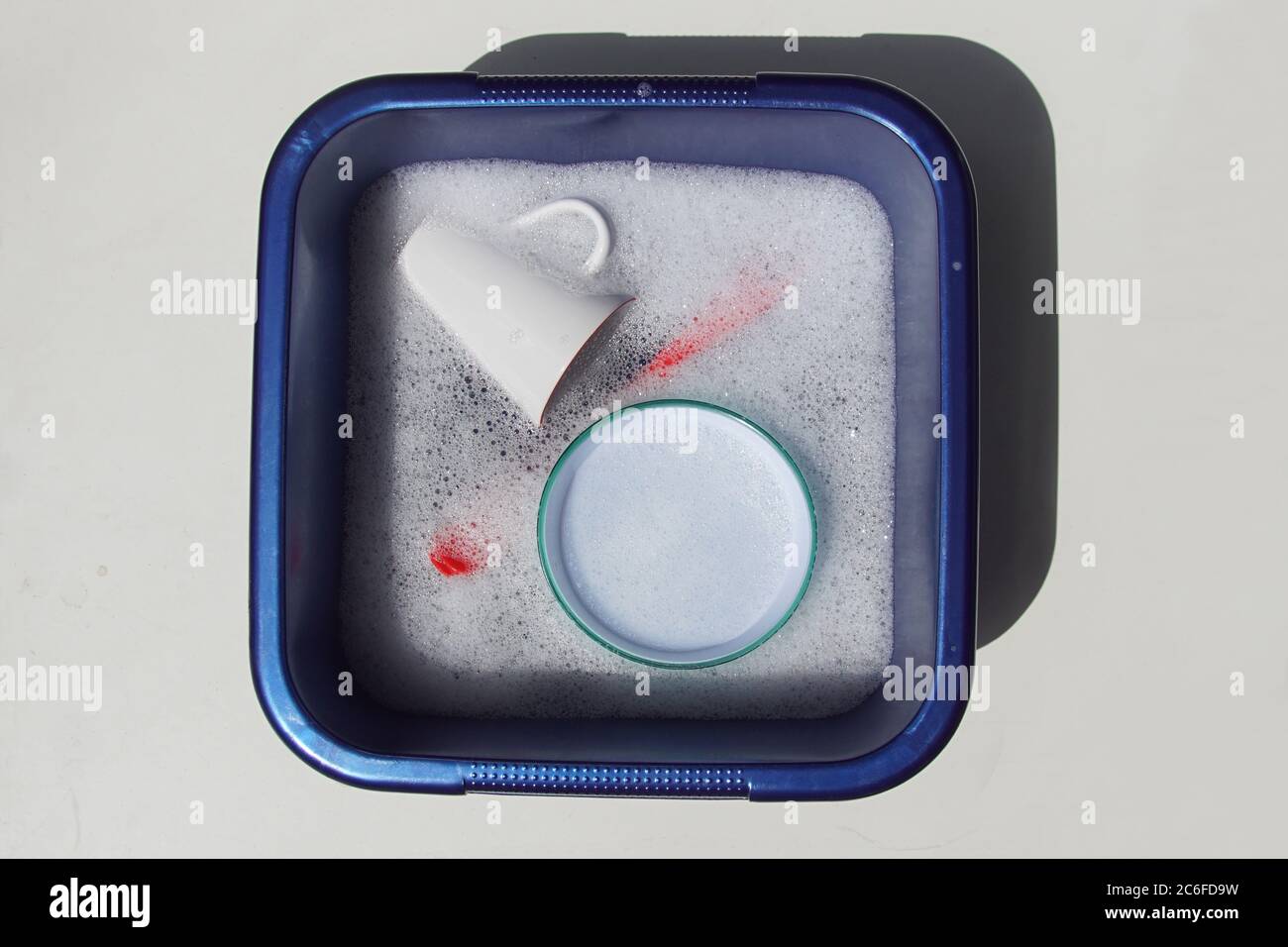 A dishwashing brush, a cup and a bowl in a blue plastic washing-up bowl ...