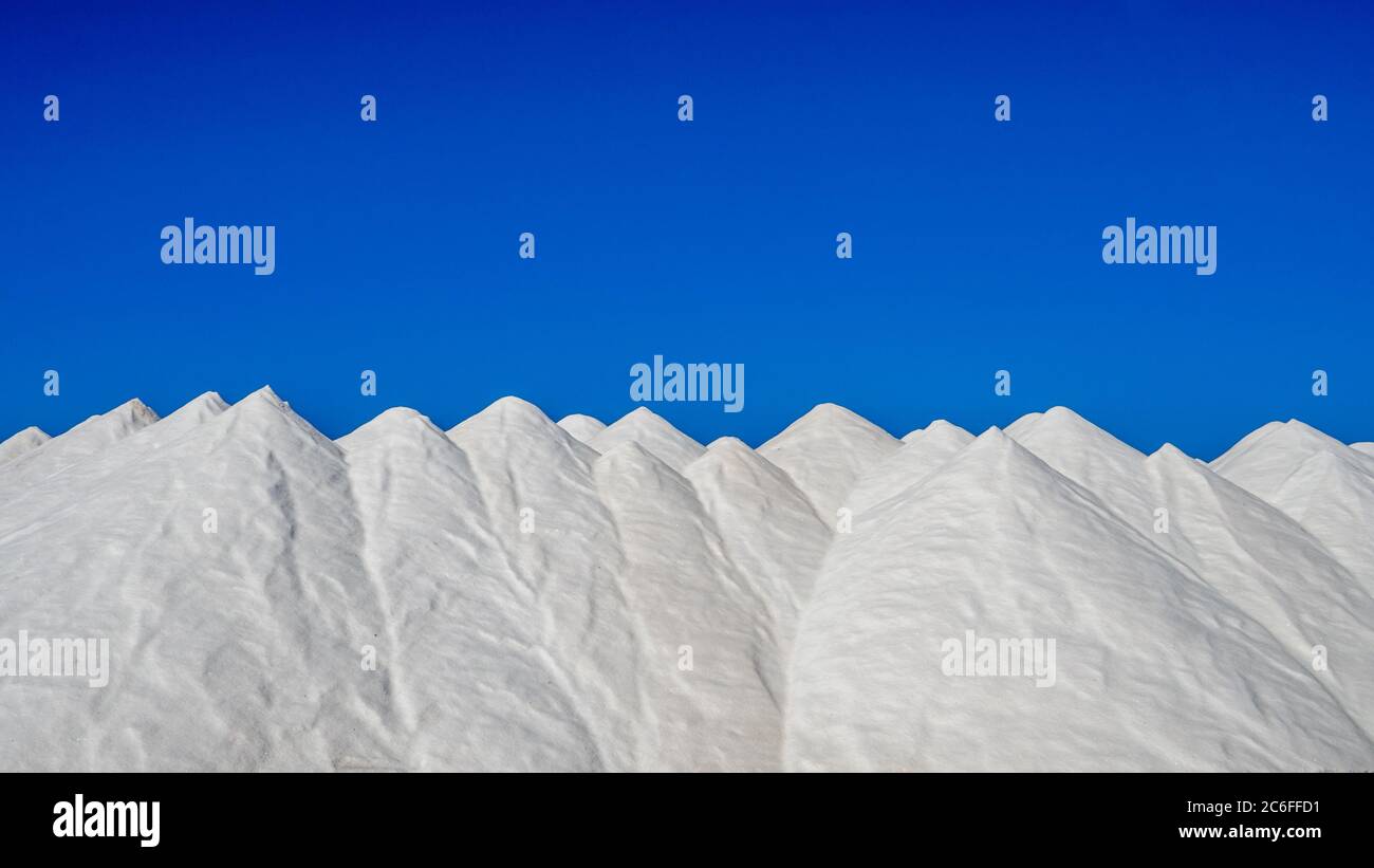 huge white hills of dried clean sea salt in front of clear blue sky and ...