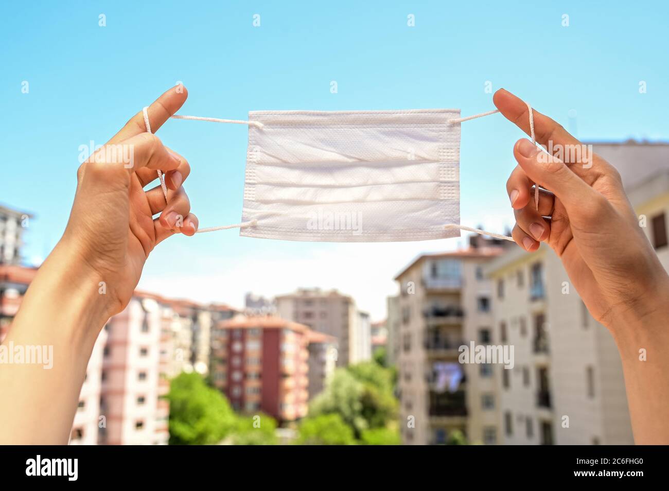 Woman holds a disposable face mask against to blue sky. Concept photo ...