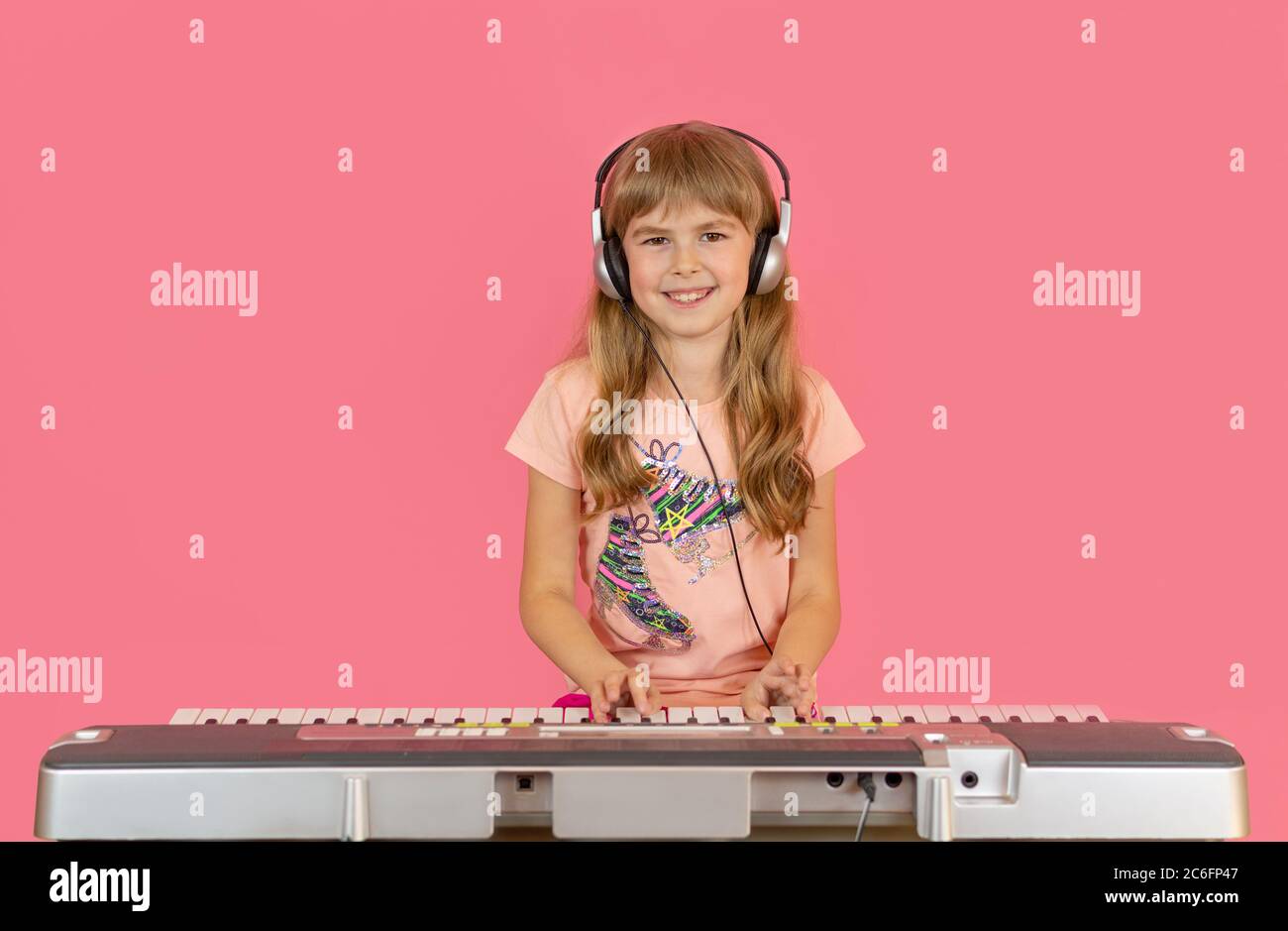 Little girl plays the synthesizer. Cheerful child on a pink background ...